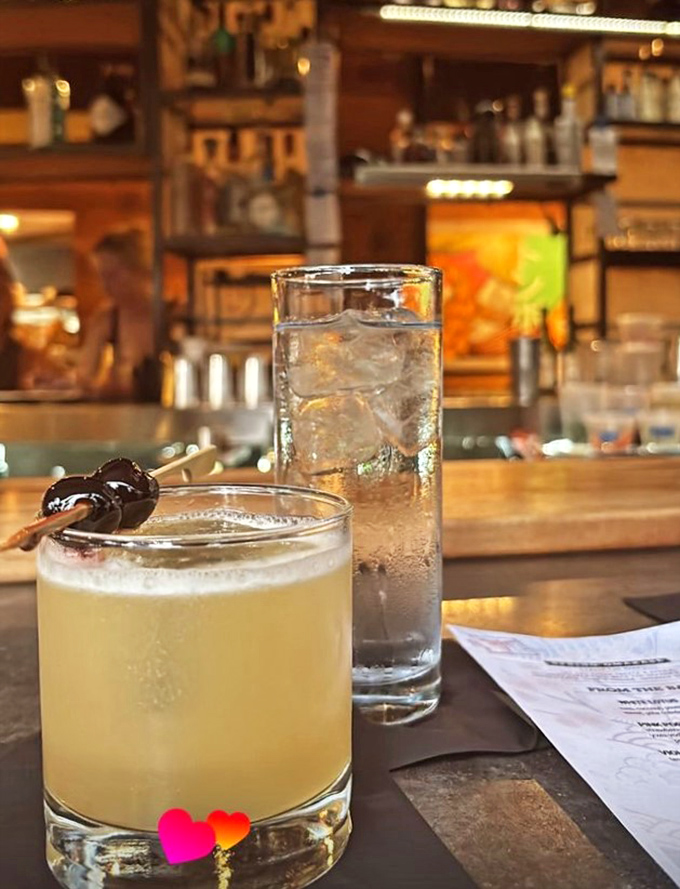 Liquid artistry in glasses &ndash; one whiskey-hued cocktail garnished with dark cherry, another tall and refreshing with promise.