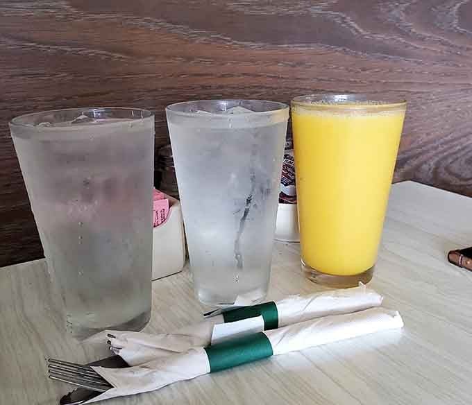 Fresh orange juice and ice water standing ready to wash down whatever breakfast masterpiece you've ordered, because proper hydration matters even when you're indulging.