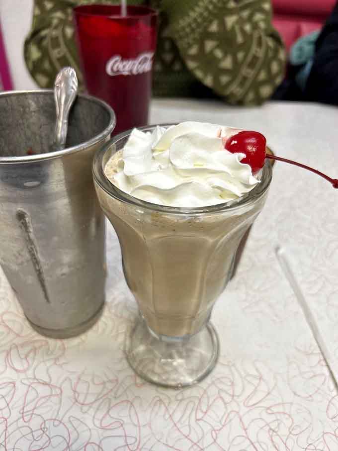 This hot fudge shake defies gravity with its whipped cream tower, crowned with a cherry that's living its best life.