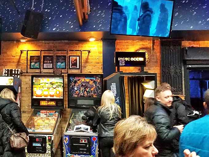 Patrons gather around vintage pinball machines, their faces illuminated by the glow of backglass art &ndash; a scene unchanged since the golden age of arcades.