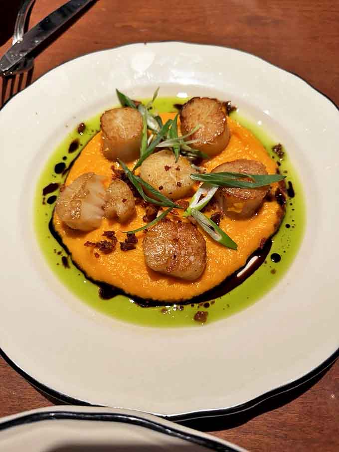 Seared scallops perch atop a vibrant orange puree, surrounded by a moat of herb-infused oil that's practically drinkable.