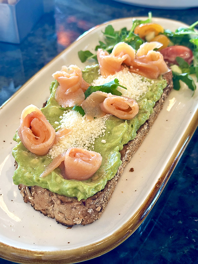 Avocado toast elevated beyond basic status with delicate salmon roses and a sprinkle of cheese – proof that sometimes trendy foods deserve their Instagram fame.