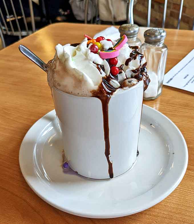 This hot chocolate transcends mere beverage status &ndash; it's a dessert in disguise, topped with whipped cream, chocolate drizzle, and colorful surprises.