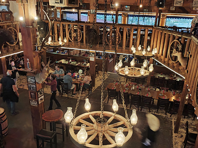 The multi-level dining room buzzes with energy – wagon wheel chandeliers cast warm light over happy diners enjoying the full Western experience.