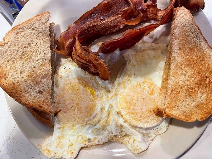 Breakfast perfection: eggs with golden centers, bacon achieving that ideal crisp-chewy balance, and toast buttered all the way to the edges.