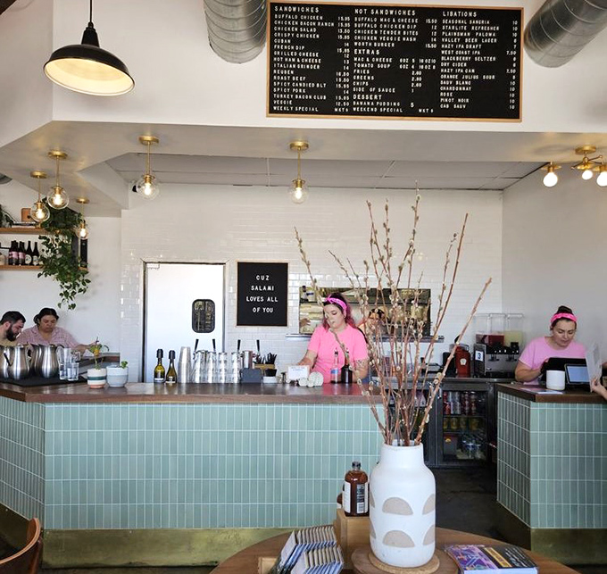 The mint-tiled command center where sandwich magic happens &ndash; staff in pink create culinary joy beneath a menu of possibilities.