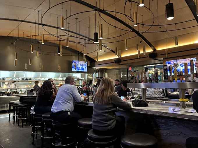The sleek bar area features modern pendant lighting and an open kitchen view, perfect for solo diners or pre-dinner cocktails.