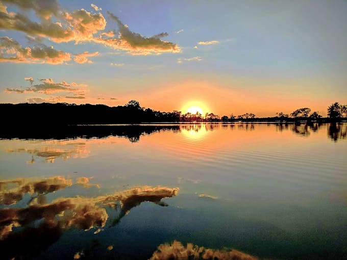 Sunset paints the sky in impossible colors while clouds drift across the water's mirror, creating a scene too beautiful for words.