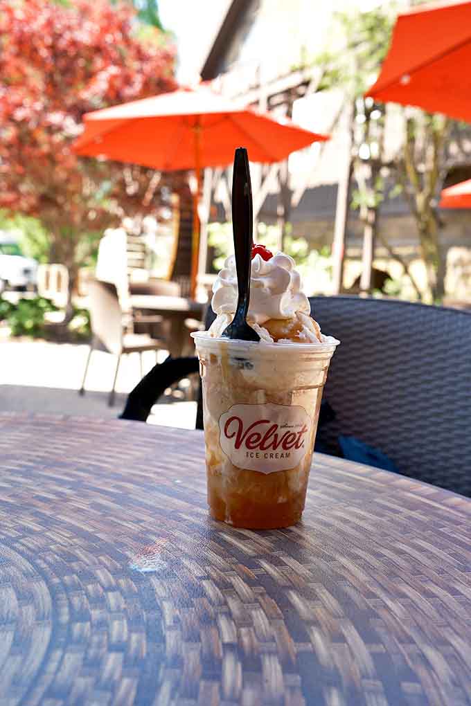 Summer perfection in a cup &ndash; caramel swirls through vanilla ice cream topped with cloud-like whipped cream against a backdrop of outdoor seating.