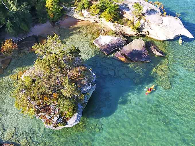 Aerial views reveal the stunning clarity of Lake Huron's waters, where kayakers appear to float above the sandy bottom near limestone formations.