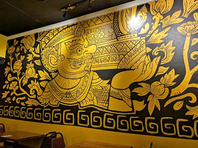 The striking gold-on-black mural depicts traditional Thai imagery, offering diners a visual feast that complements the culinary one.