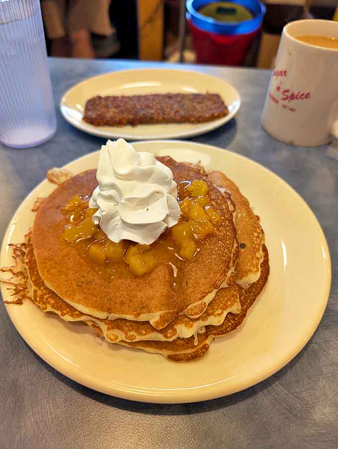 These pancakes wear their peach topping and whipped cream crown with the confidence of breakfast nobility.
