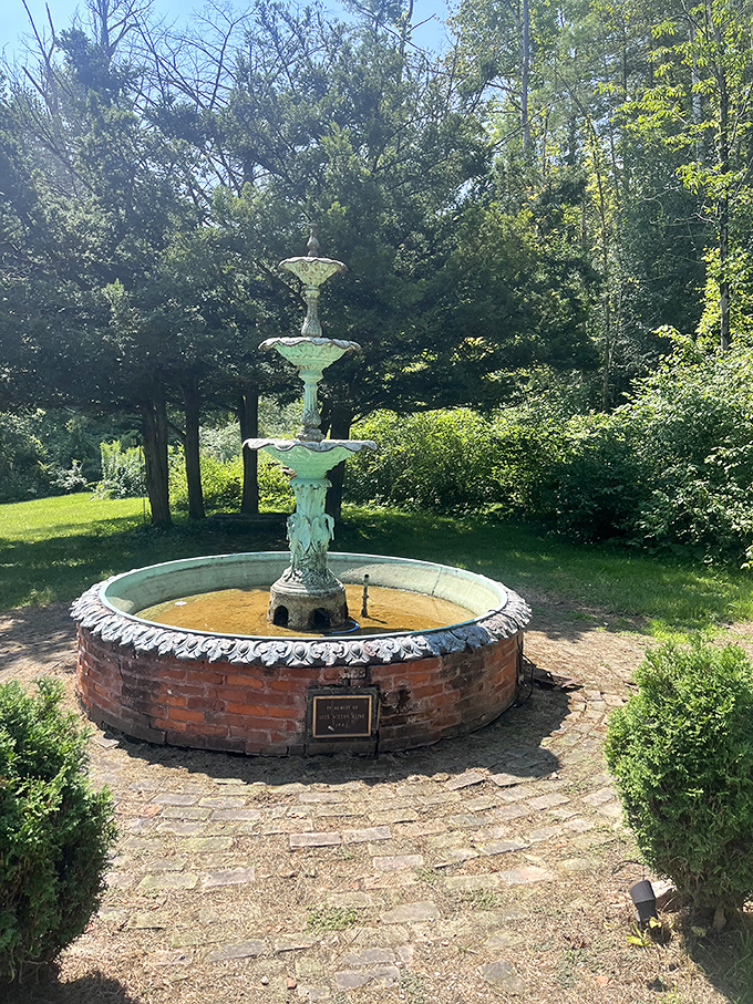The fountain stands as a weathered sentinel in the gardens, having survived more Vermont winters than most of us have survived Monday mornings.