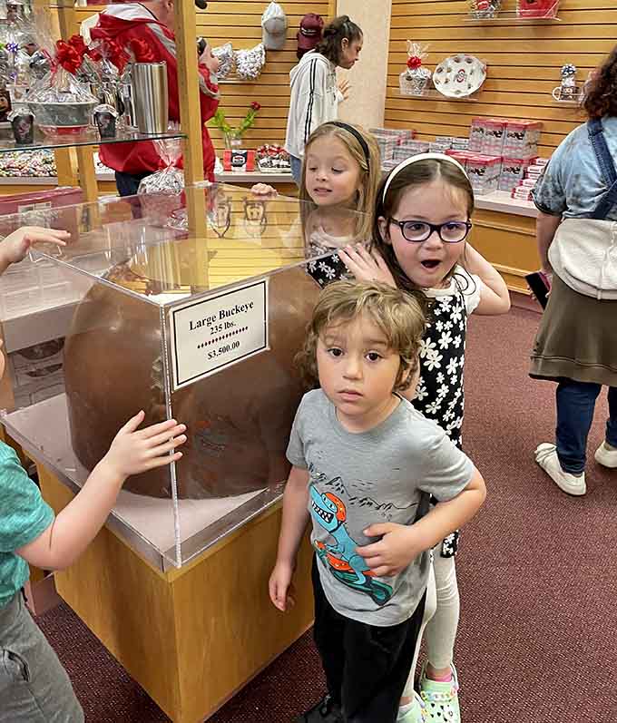 Children marvel at a massive 235-pound chocolate buckeye candy, while a young boy stands nearby, looking toward the camera curiously.