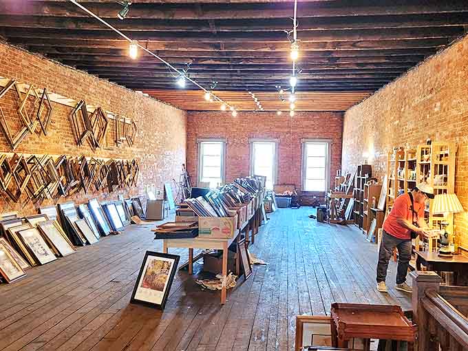 A gallery of empty frames awaits new purposes in this brick-walled sanctuary, where afternoon light streams through windows onto possibilities.
