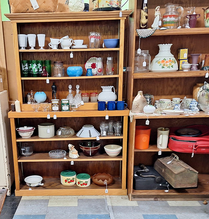 Vintage dishware and kitchen collectibles line these wooden shelves, from delicate glassware to sturdy enamelware in classic colors.