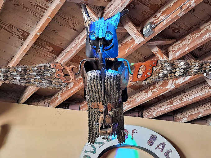 A mechanical owl spreads its bottle-cap wings beneath rough-hewn beams, its glowing blue eyes seemingly following visitors through the space.