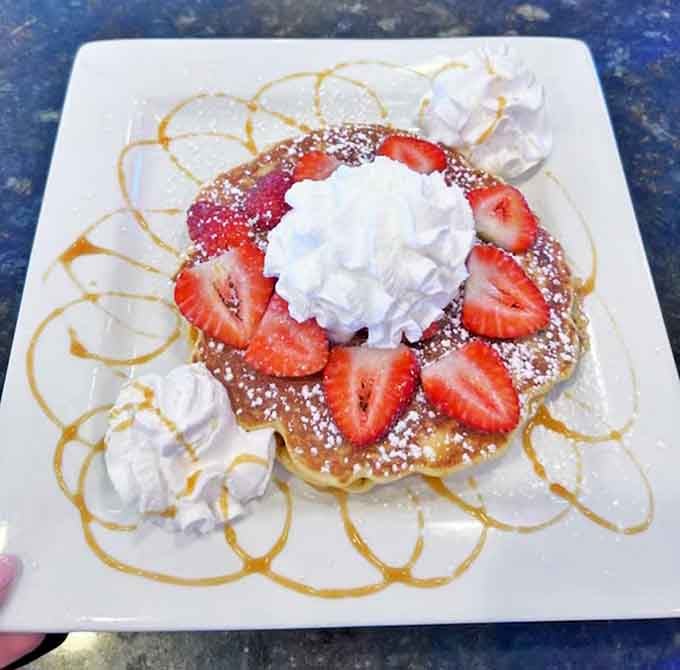 A strawberry pancake that's basically breakfast dessert &ndash; complete with artistic caramel drizzle and strategically placed whipped cream dollops.