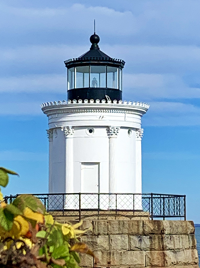 The pristine white lighthouse tower stands in elegant contrast to the blue sky, its classic design embodying New England maritime tradition.