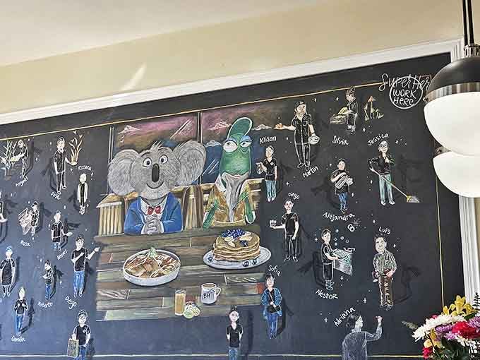 The whimsical chalkboard mural features cartoon characters enjoying breakfast alongside caricatures of the beloved staff.