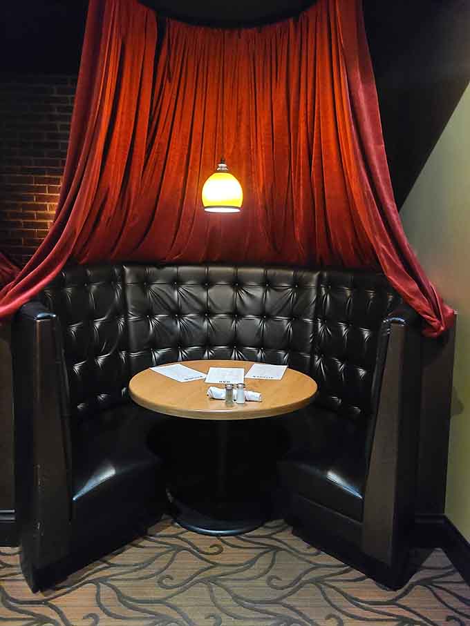 Intimate booths draped with theatrical curtains create private spaces perfect for romantic dinners or important conversations.