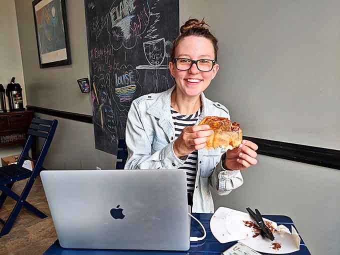 The universal language of joy: a person enjoying a French pastry while multitasking with technology&mdash;proof that priorities are in perfect order.