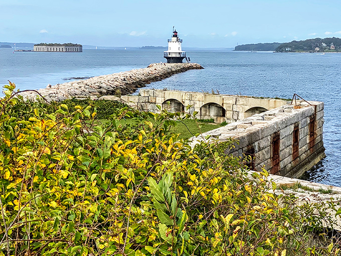 Spring Point Ledge Lighthouse creates a postcard-worthy scene with Fort Gorges visible in the distance across the sparkling bay.