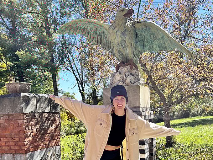 In front of the eagle statue, visitors smile for a picture, with trees and a green field stretching behind.