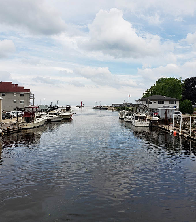 Boats line Algoma's peaceful harbor channel, where the red lighthouse beacon guides mariners safely home at day's end.