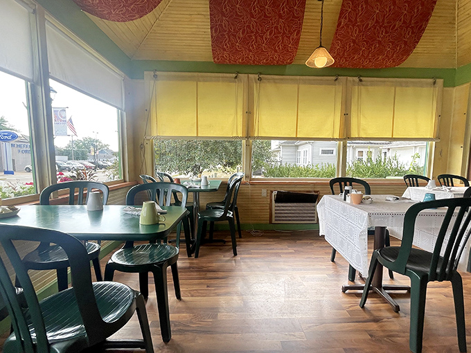 Sun-drenched windows and cheerful green chairs create a bright corner perfect for savoring coffee and watching the world go by.