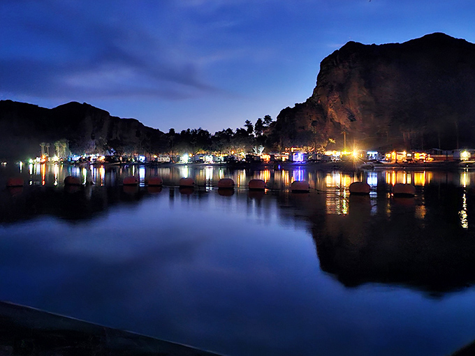 As darkness falls, riverside campsites transform into a twinkling village, their lights dancing across waters black as desert midnight.