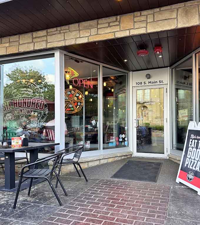 The entrance welcomes you with neon pizza signs and outdoor seating, promising good times and even better food just inside.