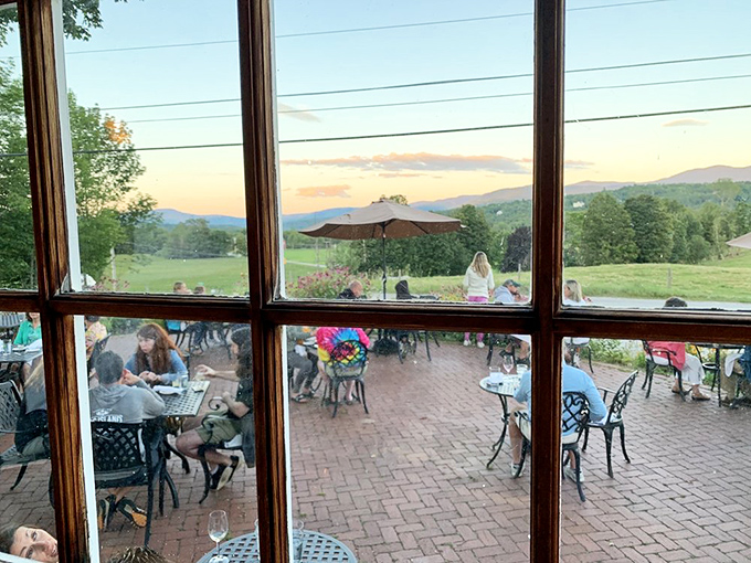 As evening falls, the view from inside captures diners enjoying the outdoor patio&mdash;a scene that epitomizes Vermont's magical summer evenings.