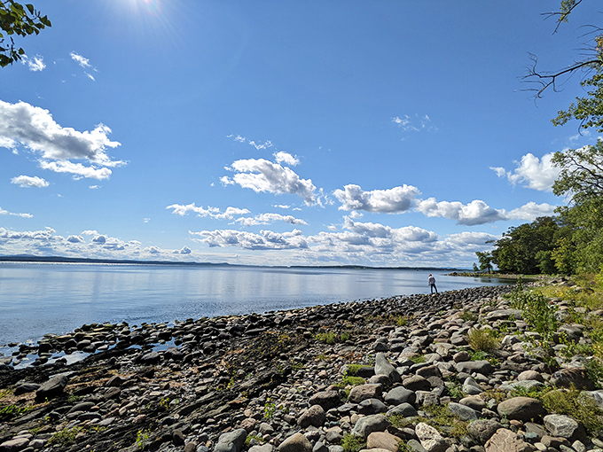 The rocky shoreline creates a perfect foreground for Lake Champlain's expansive waters and distant mountain silhouettes.