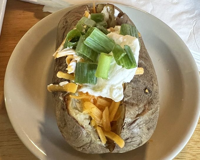A loaded baked potato that's a meal unto itself &ndash; fluffy interior topped with cheese and green onions, proving simple ingredients can create extraordinary flavors.