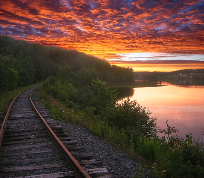 As day surrenders to dusk, the railroad tracks curve alongside a lake painted in sunset hues &ndash; nature's grand finale to a perfect day of rail adventure.