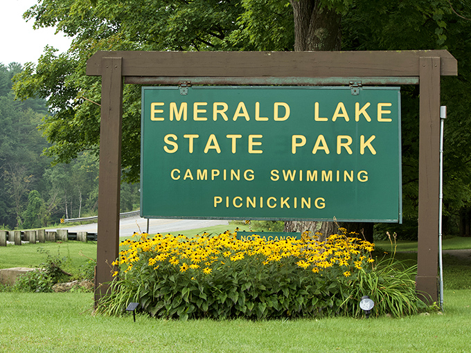 Sunshine yellow blooms frame this welcoming sign, promising three perfect Vermont pleasures: camping, swimming, and picnicking in emerald paradise.