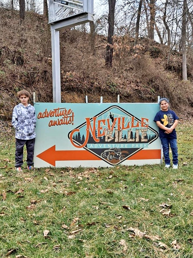 Two young adventurers flank the colorful NevilleBillie sign, their clean clothes suggesting they haven't yet experienced the park's famous mud baptism.