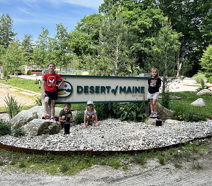 Children pose by the Desert of Maine sign, creating vacation memories that will definitely stand out from typical Maine lighthouse photos.