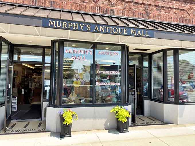 The welcoming storefront of Murphy's Antique Mall, where bright yellow flowers greet visitors about to embark on a journey through America's material past.