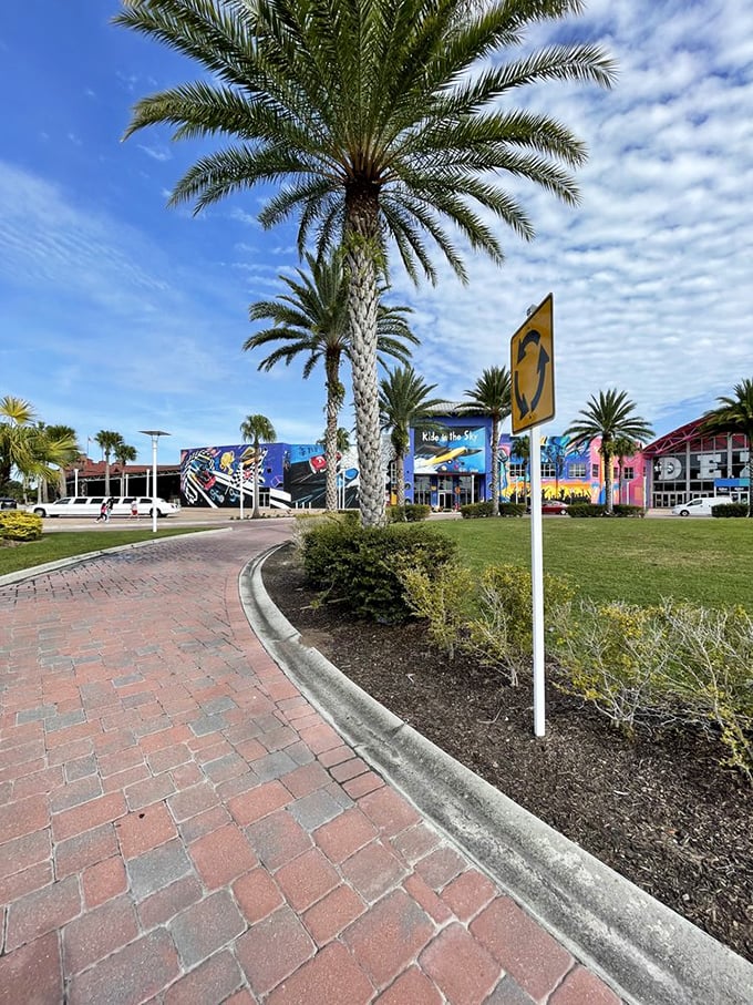 Palm trees stand sentinel along the brick pathway, whispering promises of air-conditioned adventures awaiting inside.