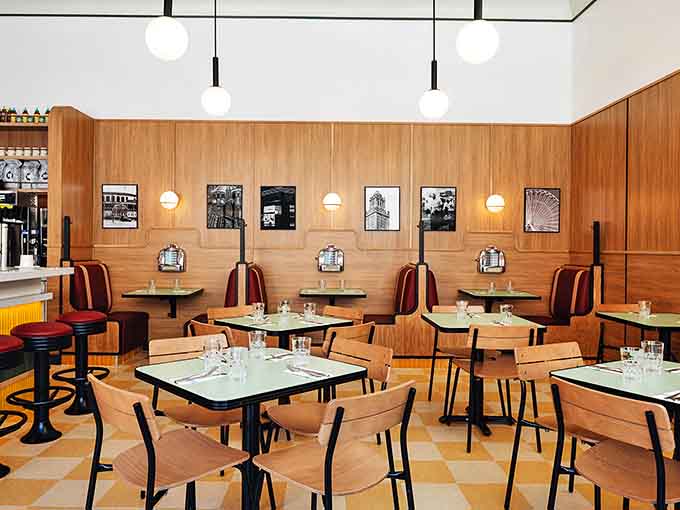 Warm wood paneling meets mid-century modern design in this stylish interior where checkerboard floors and cozy booths create the perfect dining atmosphere.