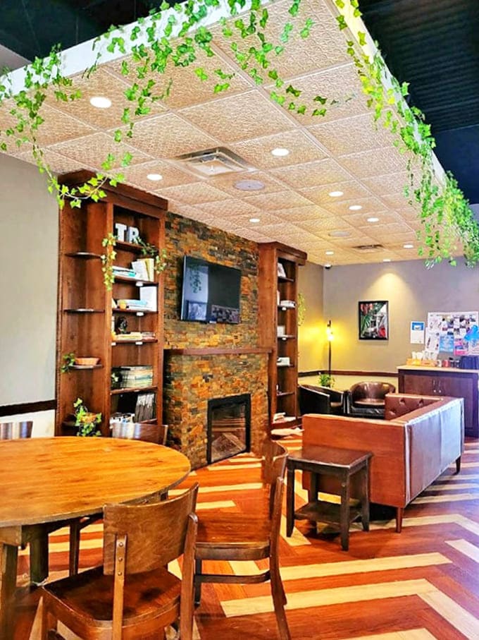 Cascading ivy adorns the ceiling above a stone fireplace and wooden bookshelves, creating a living room vibe that makes laptop warriors and book lovers equally at home.