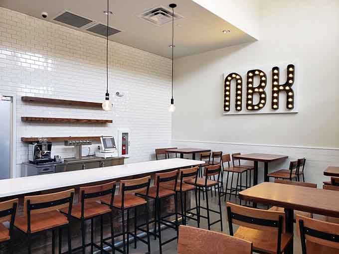 Clean lines and warm wood tones create an inviting space where the "NBK" sign winks at you like it knows something delicious is about to happen.