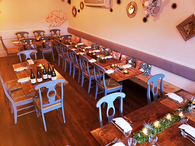 Long wooden tables and blue chairs create a convivial atmosphere where strangers become friends over shared plates and flowing conversation.