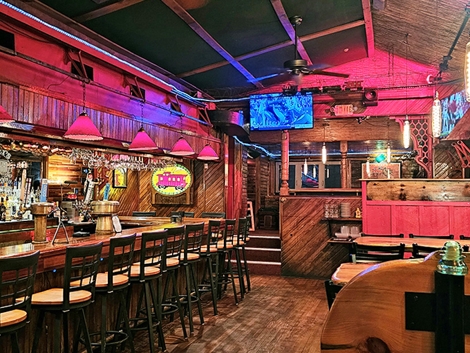 Step inside to a warm wooden wonderland where red lighting casts a glow that makes the bar area feel like a cozy cabin retreat.