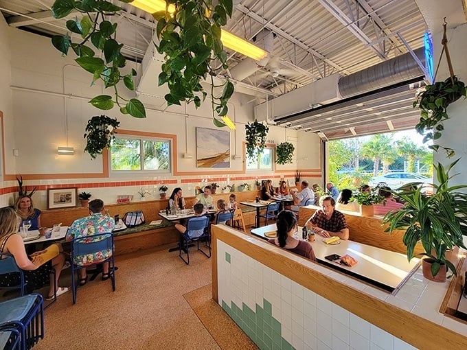Inside Whitney's, hanging plants create a lush canopy above diners while natural light floods the space – botanical chic meets vintage Florida cool.