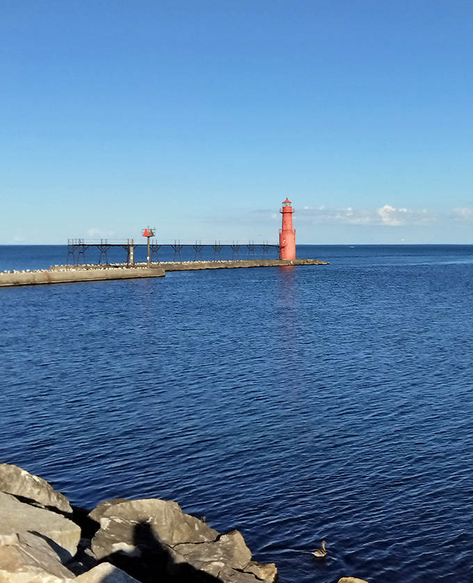 The iconic red Algoma Pierhead Lighthouse stands sentinel at the harbor entrance, a splash of color against the deep blue horizon.