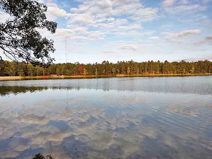 Mirror-like waters reflect clouds and surrounding pines, creating that rare perfect symmetry that makes amateur photographers look like professionals.