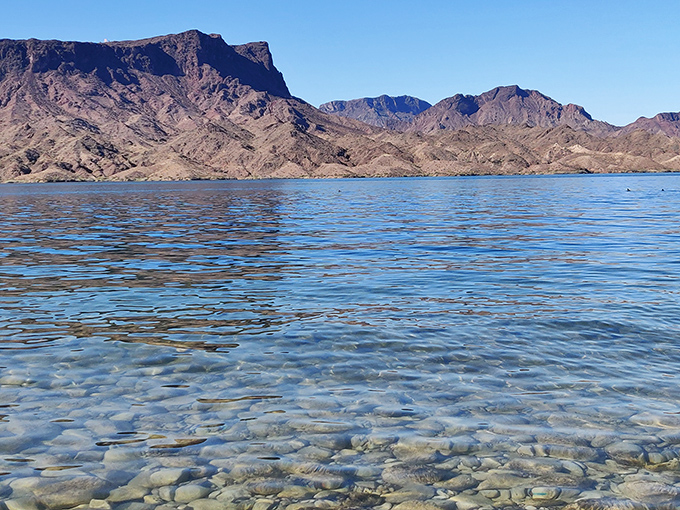 The glassy surface of Lake Havasu reflects rugged mountain silhouettes, creating a mirror image that doubles the visual impact of this desert oasis.